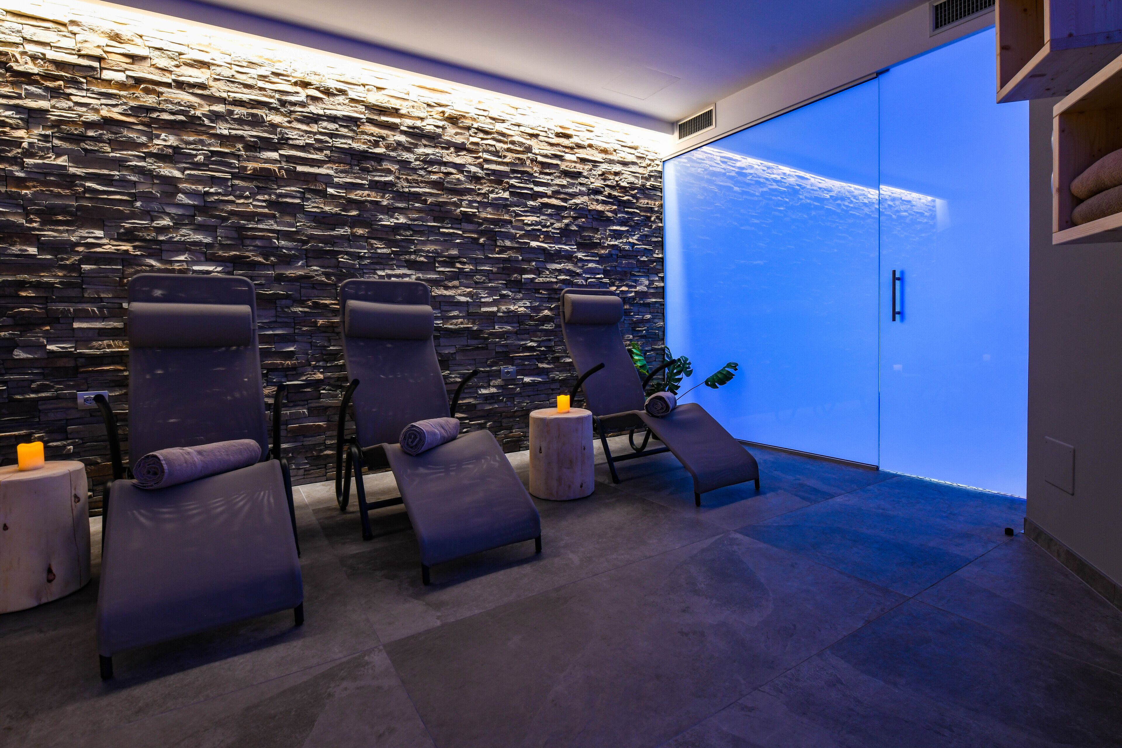 Uma área de spa com paredes de pedra, cadeiras reclináveis e uma janela ampla.