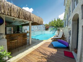 Uma área na piscina com bar, espreguiçadeiras e um telhado de palha.
