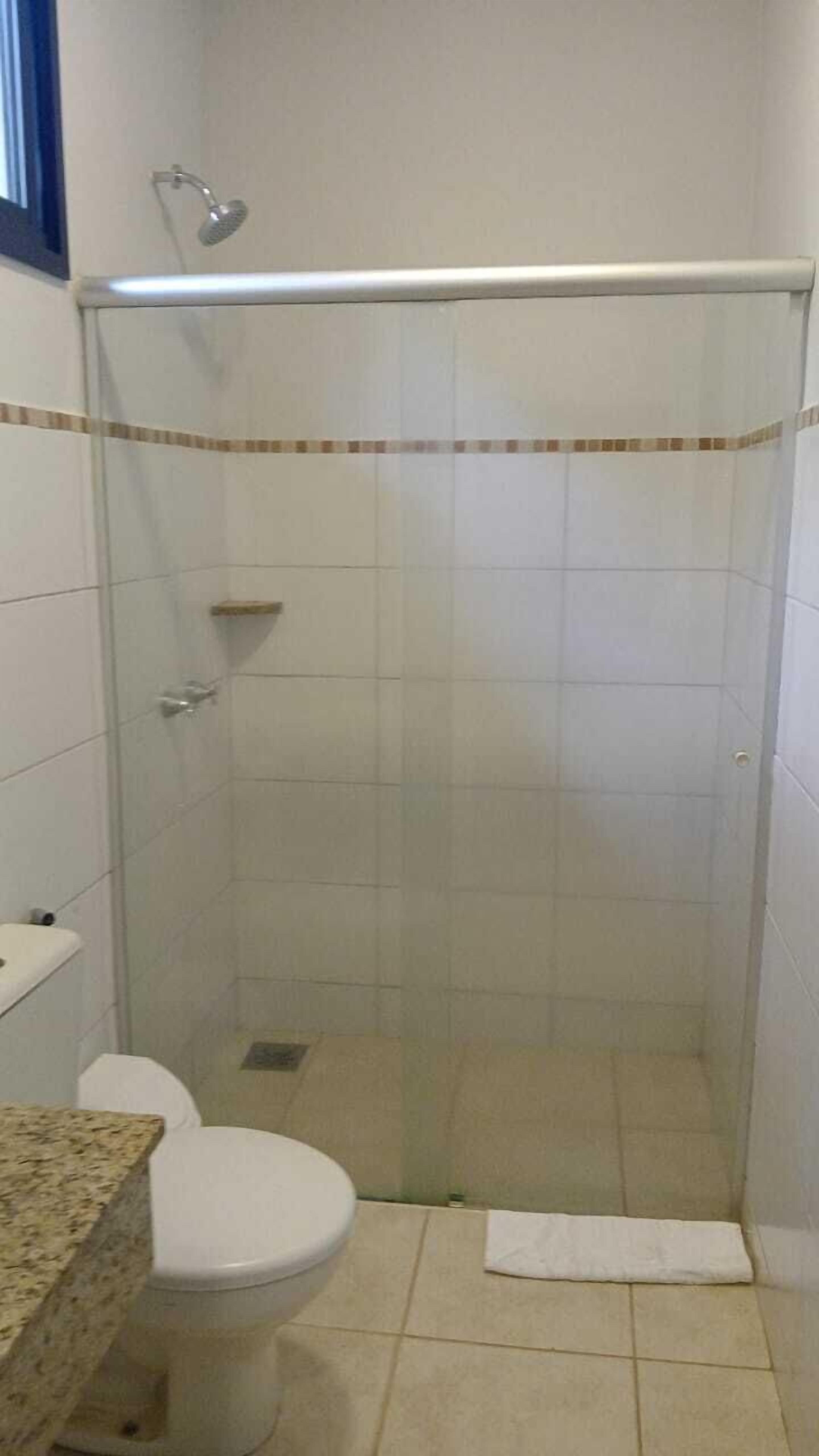 Um espaço de banho pequeno e fechado, com porta de vidro, vaso sanitário e pia.