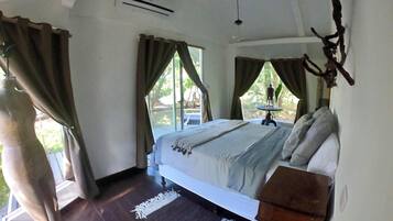 Quarto com cama, mesa de cabeceira de madeira, pequena mesa e luminária pendente.