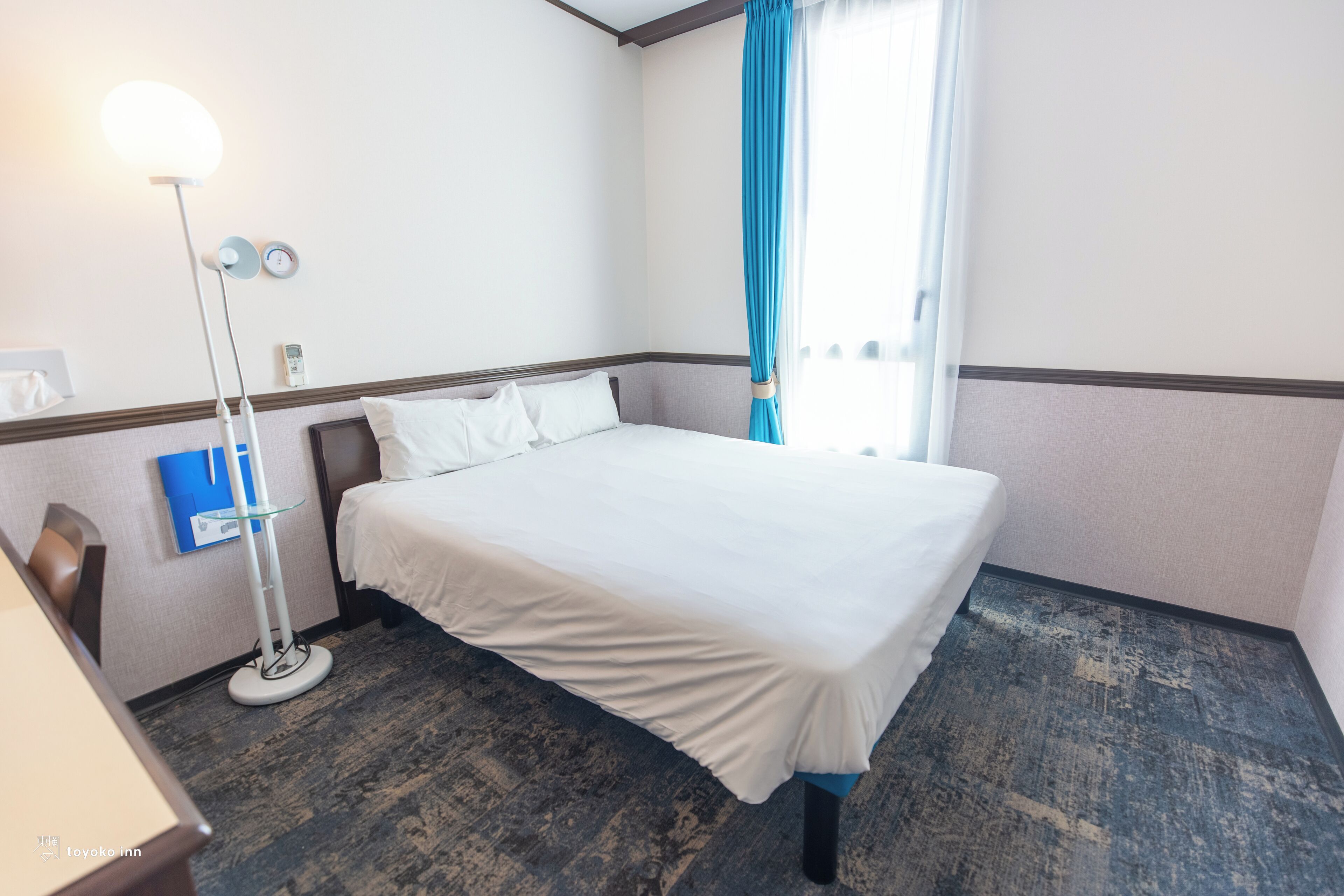 Quarto de hotel com cama, escrivaninha, abajur e vista para o exterior.