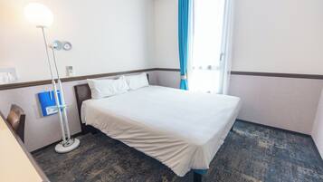 Quarto de hotel com cama, escrivaninha, abajur e vista para o exterior.
