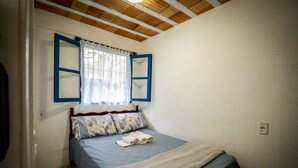 Um quarto pequeno com uma cama de solteiro, uma janela com molduras azuis e uma cortina.