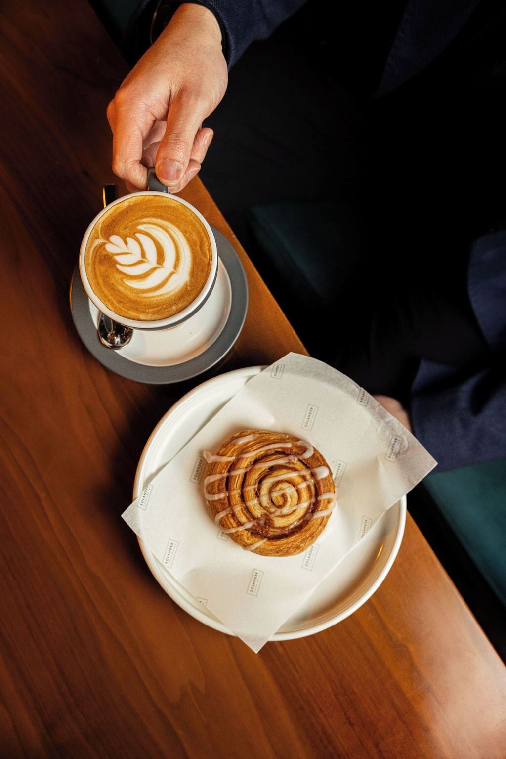 Uma mesa de madeira com uma chávena de café e um prato de rolinhos de canela.