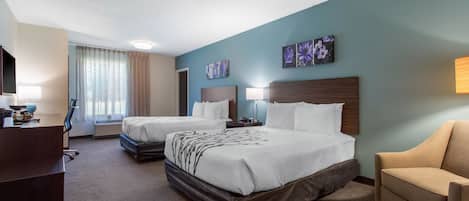 Quarto de hotel com duas camas, uma escrivaninha, uma cadeira e obras de arte nas paredes.