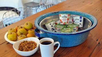 Uma mesa de café da manhã com um prato de maçãs, uma tigela de granola, uma xícara de café e uma tigela azul contendo iogurte orgânico com baixo teor de gordura e um pacote de leite.