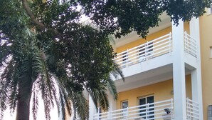 Um edifício de dois andares com varanda, plantas em vasos e área de entrada pavimentada.