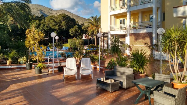 Pátio de hotel com área de estar externa, piscina e montanhas ao fundo.