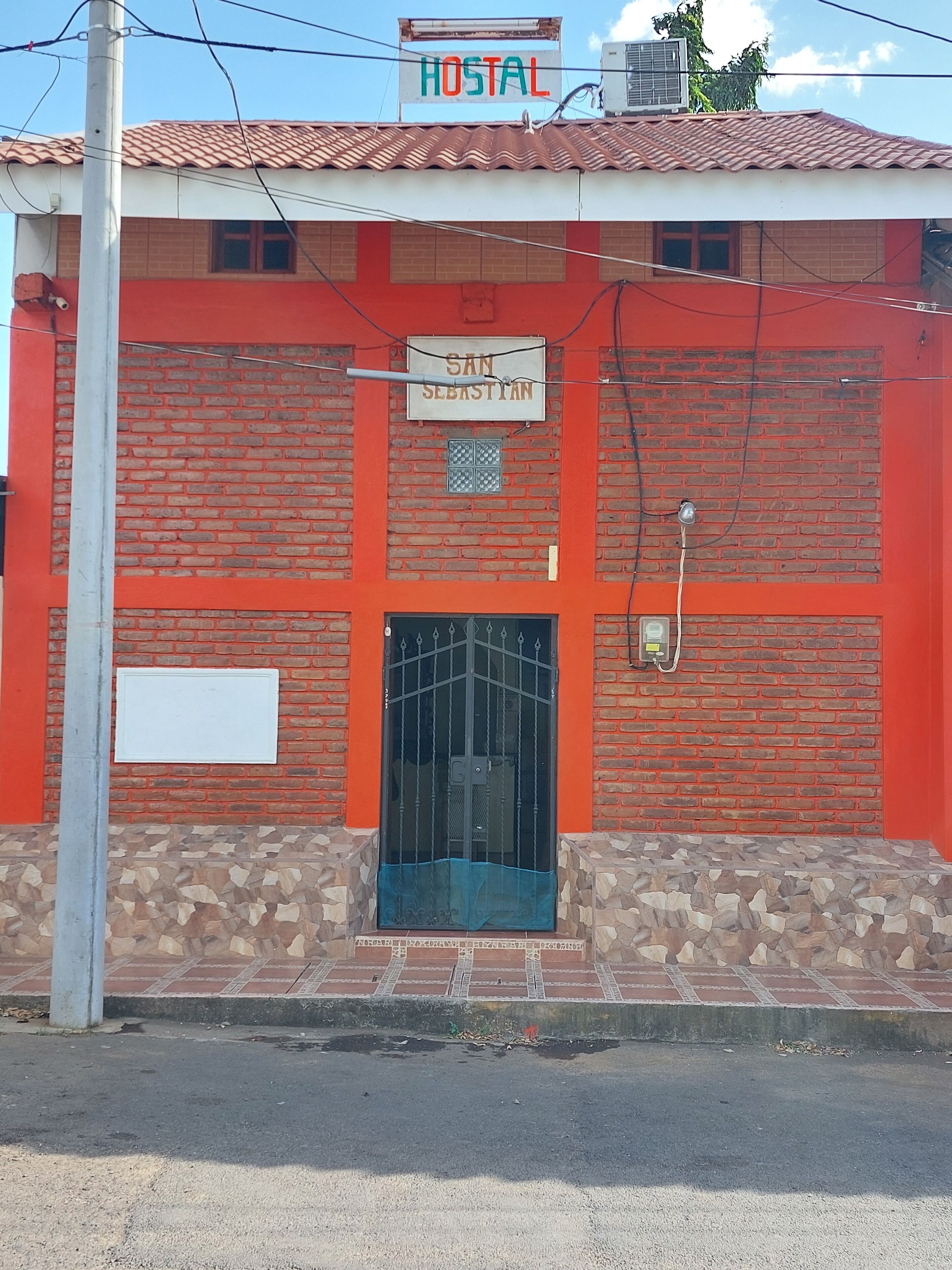 Um hostel com fachada vermelha, uma placa com a inscrição 'SAN SEBASTIAN' e entrada com azulejos.