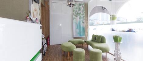Uma sala de estar moderna com piso de madeira, pufes verdes, televisão de tela plana e uma grande janela com vista para a cidade.
