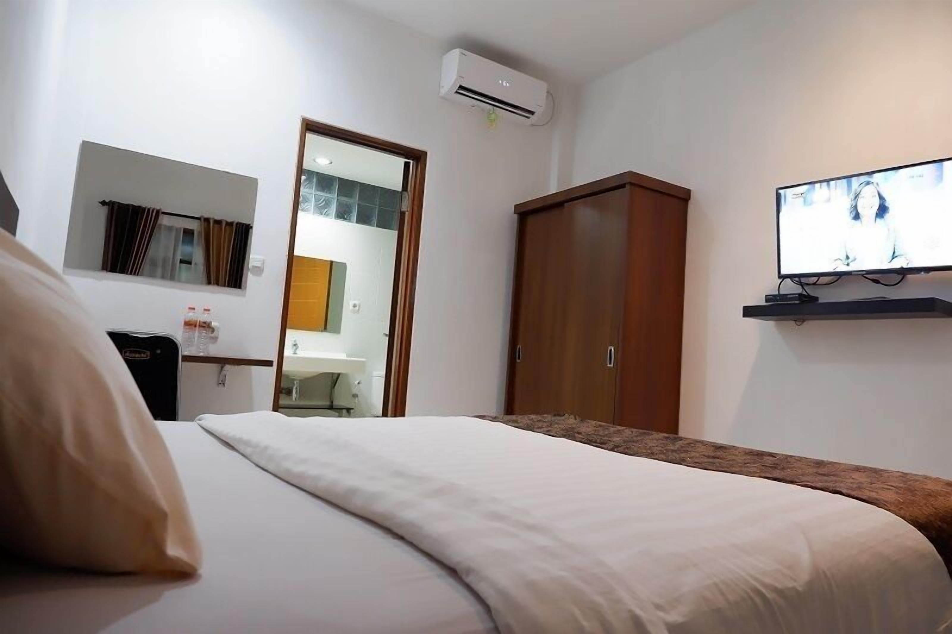Quarto de hotel com uma cama, um guarda-roupa, uma televisão e uma casa de banho visível através de uma porta aberta.