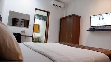 Quarto de hotel com uma cama, um guarda-roupa, uma televisão e uma casa de banho visível através de uma porta aberta.