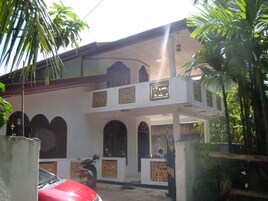 Uma casa de dois andares com varanda, janelas em arco e um carro vermelho estacionado na frente.