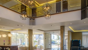Um hall espaçoso com pé-direito alto, luminárias hexagonais modernas e uma área de estar central com pufes amarelos.