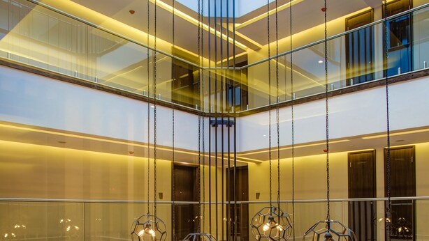 Um átrio espaçoso com pé-direito alto, luminárias hexagonais modernas e uma área de estar central com banquetas redondas.