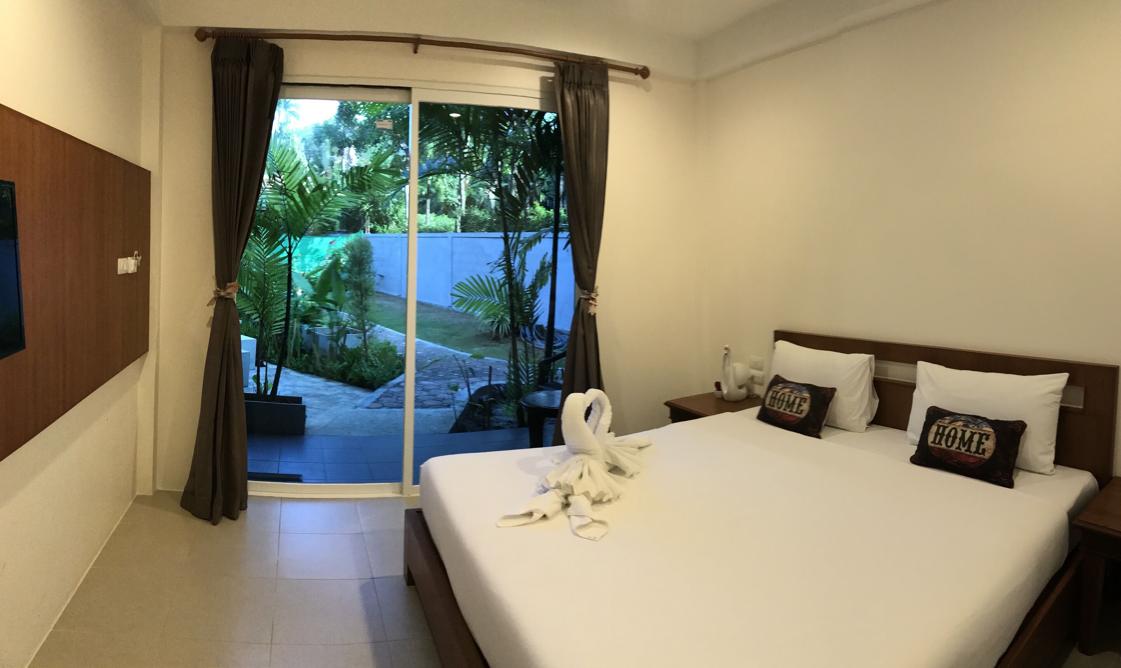 Quarto de hotel com uma cama, mesa de cabeceira, toalha e vista para um jardim através de uma porta deslizante.