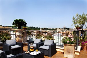Terraço no telhado com mobiliário de vime, plantas em vasos e vista para a paisagem urbana.