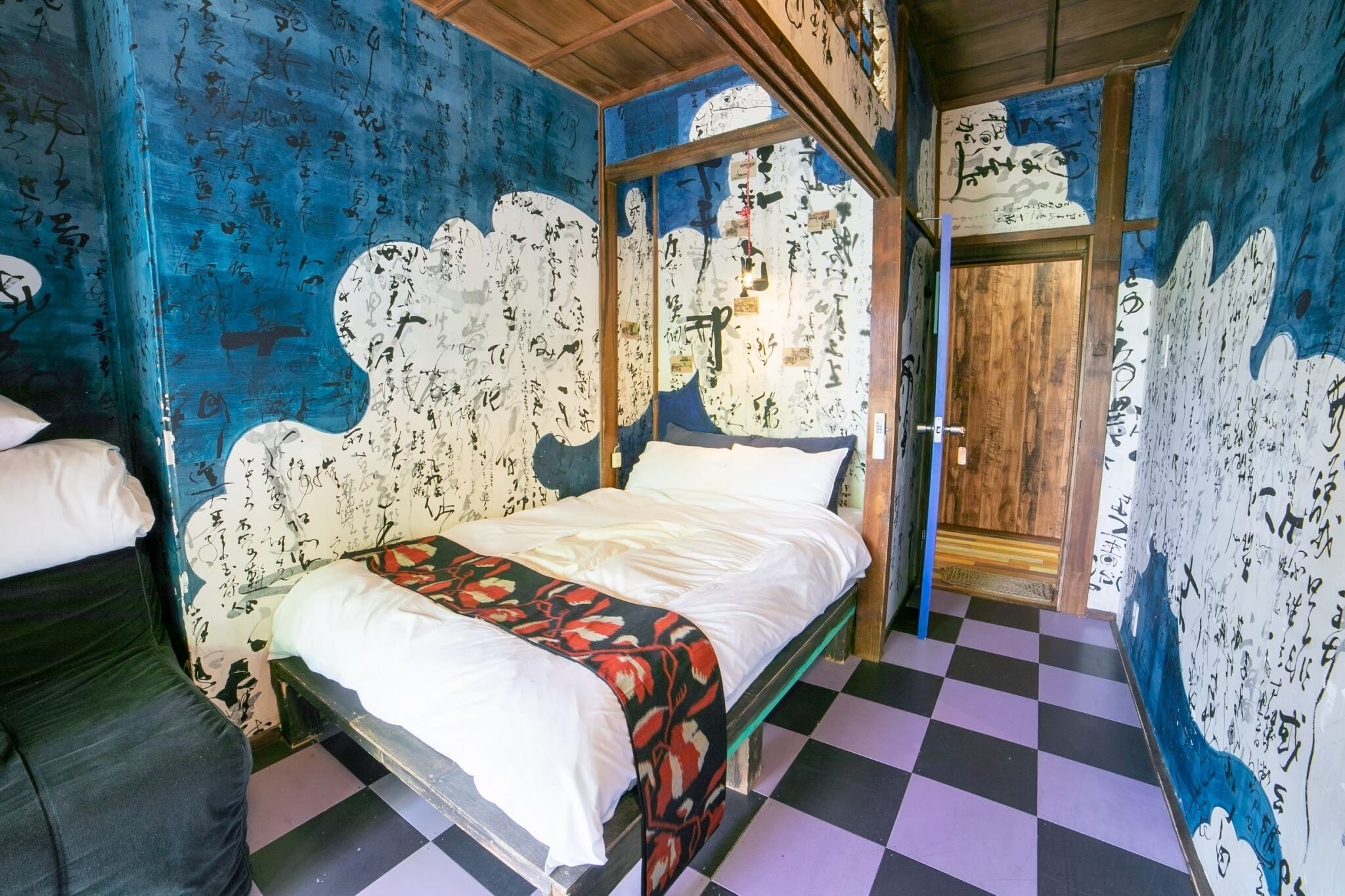 Um quarto com uma cama, uma porta de madeira e paredes decoradas com caligrafia.