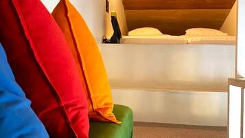 Quarto pequeno e acolhedor, com uma cama beliche, um sofá verde e almofadas coloridas, além de teto de madeira.