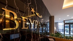 Uma área de recepção de hotel moderna, com uma parede de vidro exibindo o nome 'BEYRAM' em letras grandes.