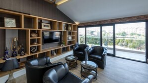 Uma sala de estar moderna com uma TV grande, sofás de couro preto e uma varanda com vista.