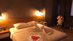 Quarto de hotel com uma cama, mesa de cabeceira, cadeira e luminária fixada na parede.