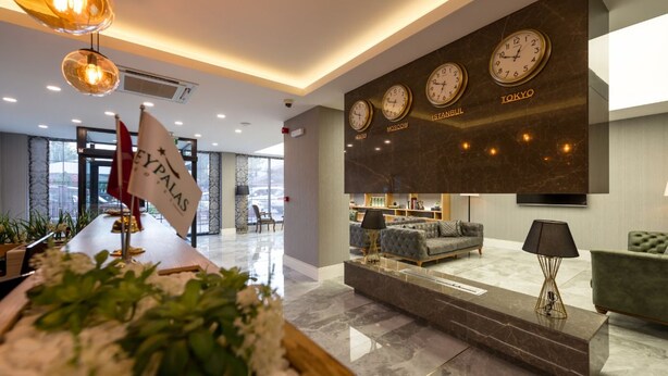 Um hall de hotel moderno com balcão de recepção, área de estar e relógios de parede mostrando os horários de Moscou, Istambul e Tóquio.