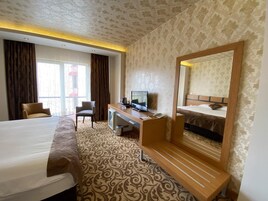 Quarto de hotel com cama, escrivaninha com televisão, uma cadeira e um espelho grande.