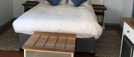 Quarto com cama, duas mesas de cabeceira, um criado-mudo, um banco de madeira e um radiador.