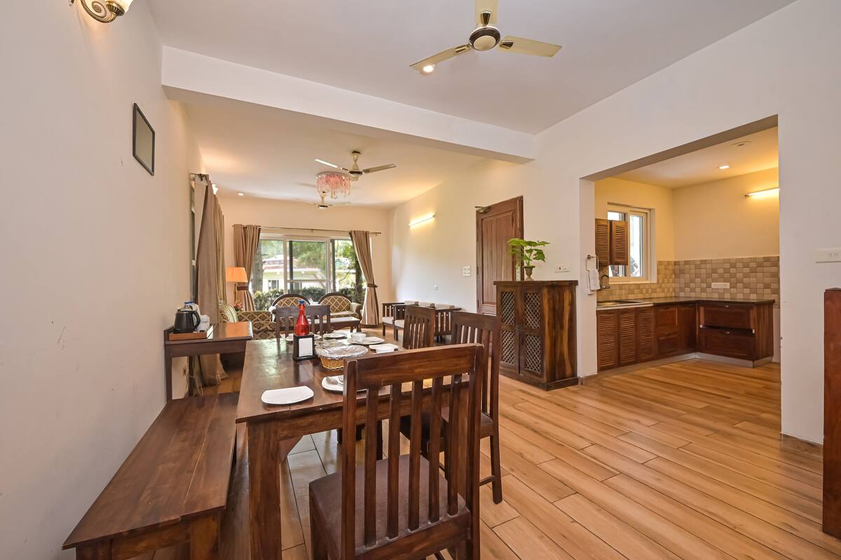 Uma sala de jantar ampla com mesa e cadeiras de madeira, ventilador de teto e vista para a cozinha.