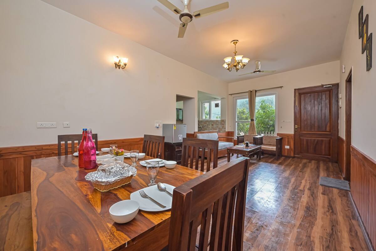 Uma sala de jantar com uma mesa de madeira posta para quatro pessoas, um ventilador de teto e um lustre.