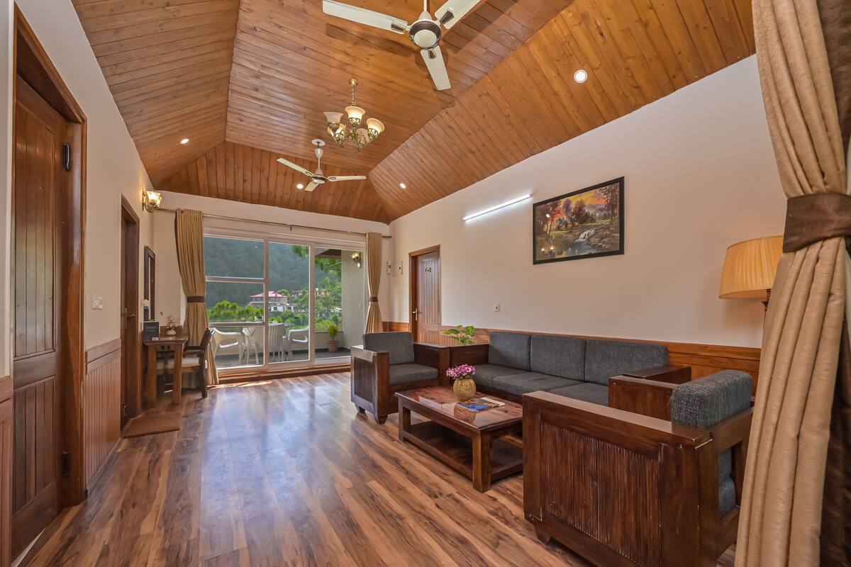 Uma sala de estar ampla com piso de madeira, um conjunto de sofás, uma mesa de centro e um ventilador de teto.