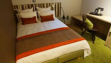 Quarto de hotel com cama, escrivaninha e cadeira.