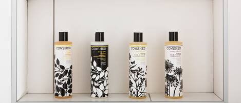 Quatro frascos de gel de banho e duche Cowshed numa vitrine branca.
