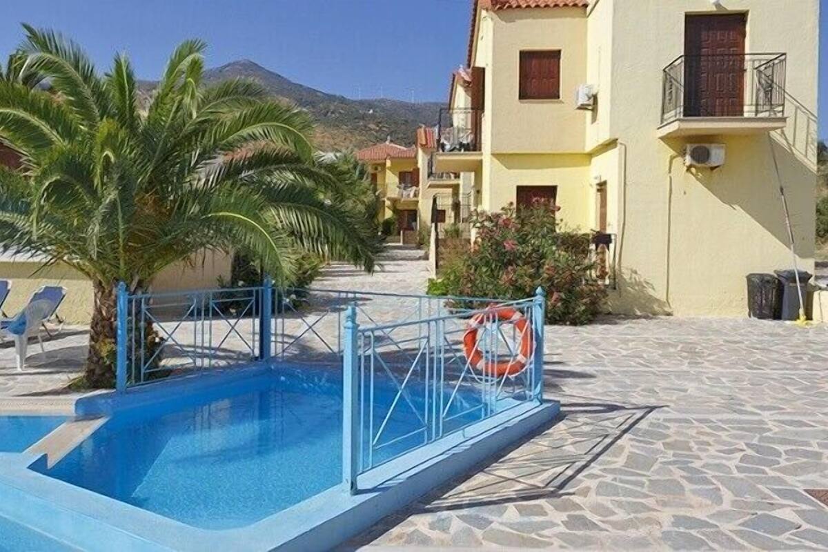 Piscina com cerca azul, palmeiras e montanhas ao fundo.
