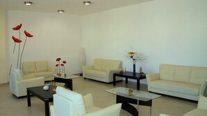 Uma sala de estar moderna com três sofás brancos, duas mesas de centro e vasos decorativos com flores.