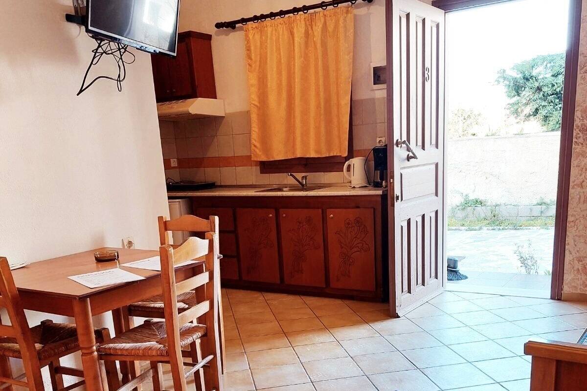Uma cozinha compacta com área de refeições, uma televisão na parede e vista para o exterior através de uma porta aberta.