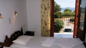 Quarto com cama, cabeceira de madeira, mesa de cabeceira e janela com vista para o mar e um carro estacionado.
