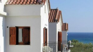Um edifício costeiro com telhado em telhas, varanda com grade de metal e vista para o mar.