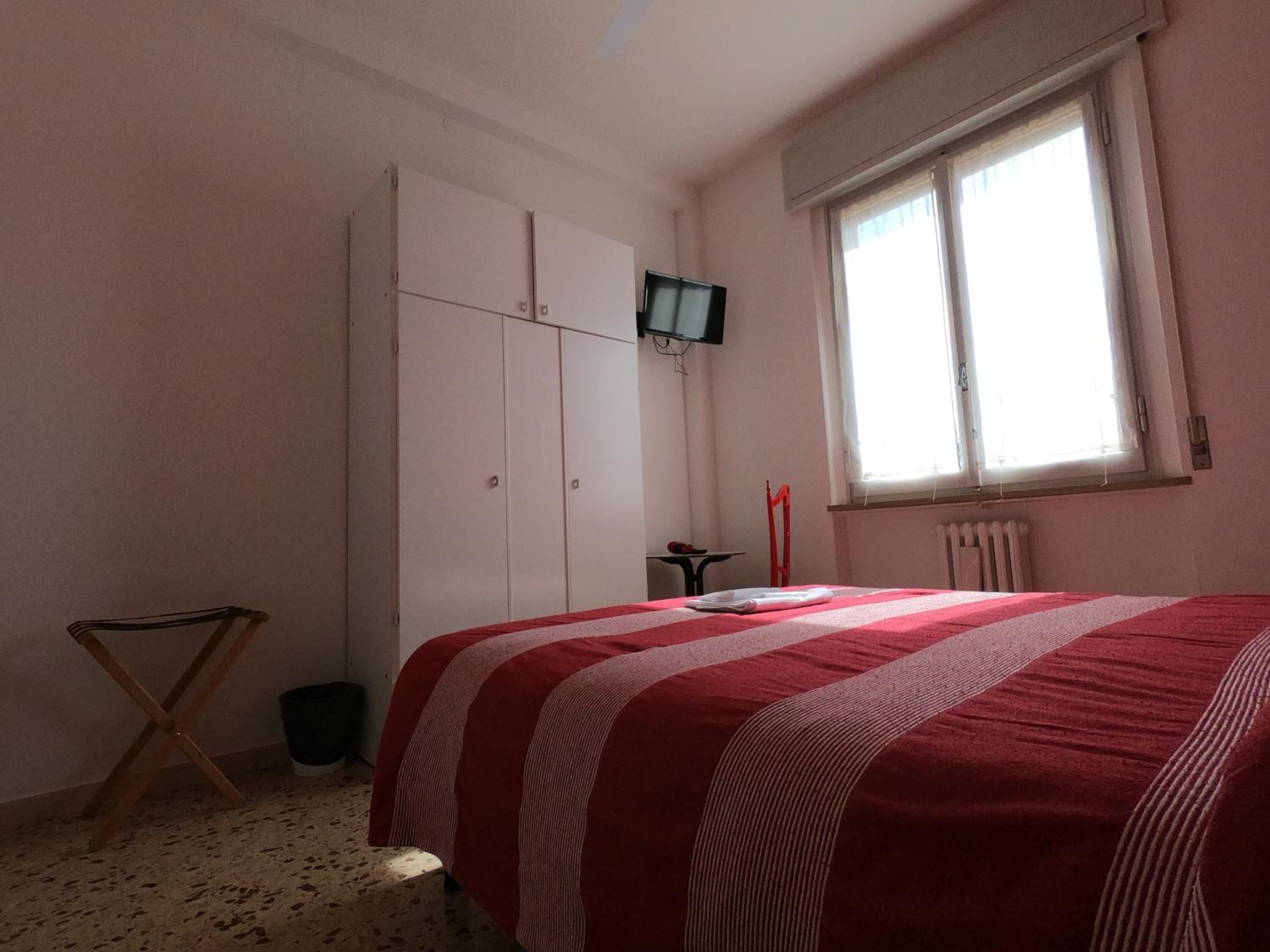 Quarto com cama, guarda-roupa, televisão e janela.
