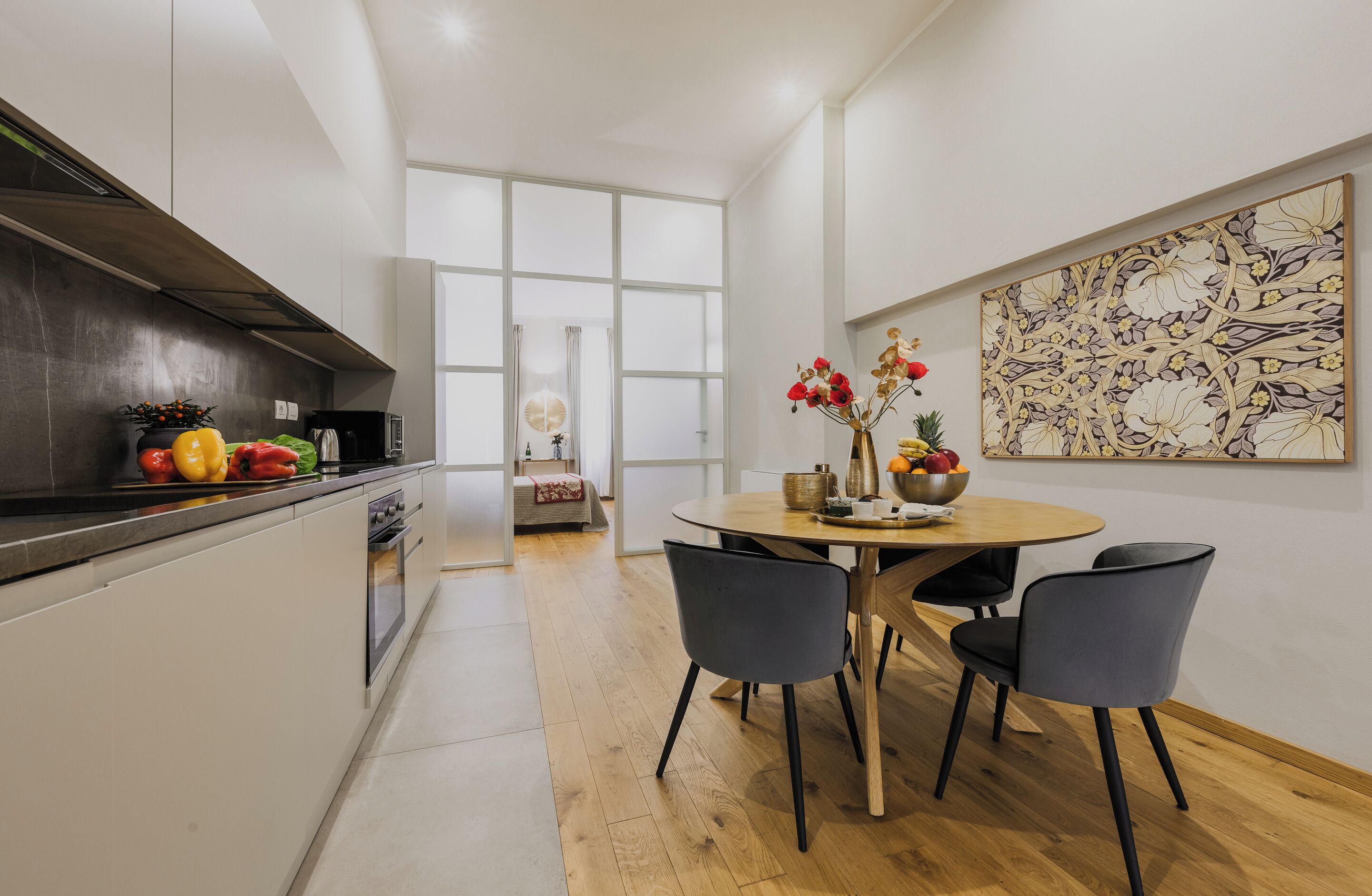 Cozinha moderna com área de refeições, apresentando uma mesa de madeira, duas cadeiras e uma grande obra de arte floral na parede.