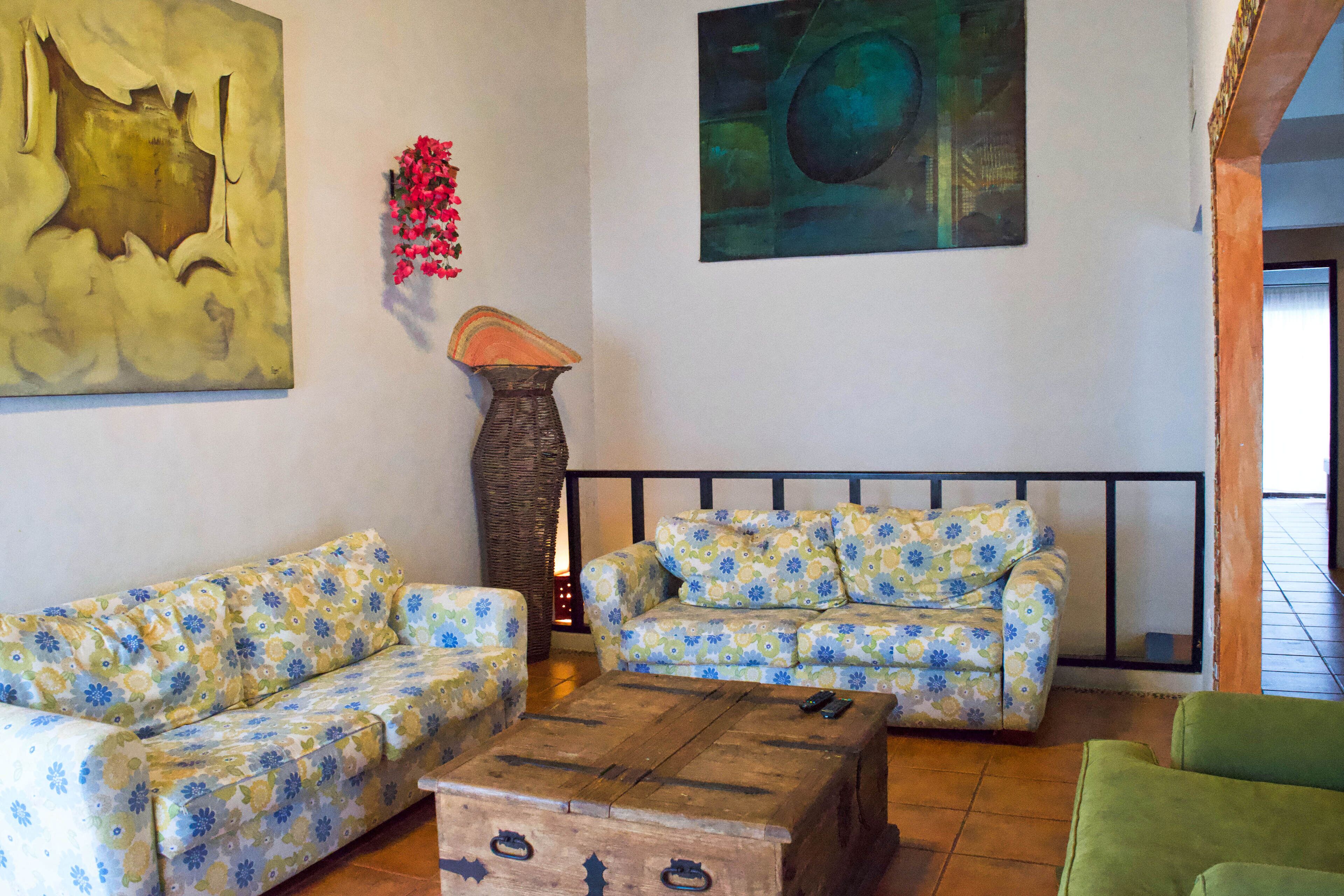 Uma sala de estar com dois sofás estampados com flores, uma mesa de centro de madeira e um vaso grande com flores vermelhas.