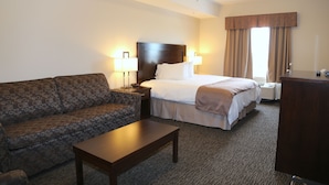 Quarto de hotel com cama, sofá, mesa de cabeceira, abajur e escrivaninha.