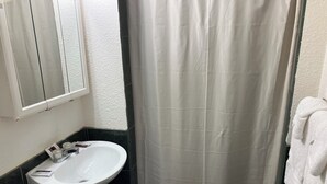 Casa de banho com lavatório branco, sanita, cortina de chuveiro e porta-toalhas.