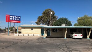 Um motel com edifício de um andar, área de estacionamento e um carro branco estacionado na frente.