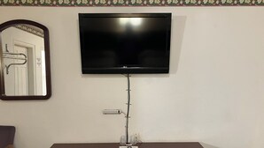 Televisão fixada na parede sobre um aparador de madeira com gavetas.