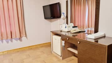 Quarto de hotel com uma secretária de madeira, televisão na parede, frigorífico pequeno e espelho.