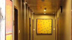 Um corredor de hotel com carpete estampado, portas em ambos os lados e uma obra de arte emoldurada na parede esquerda.