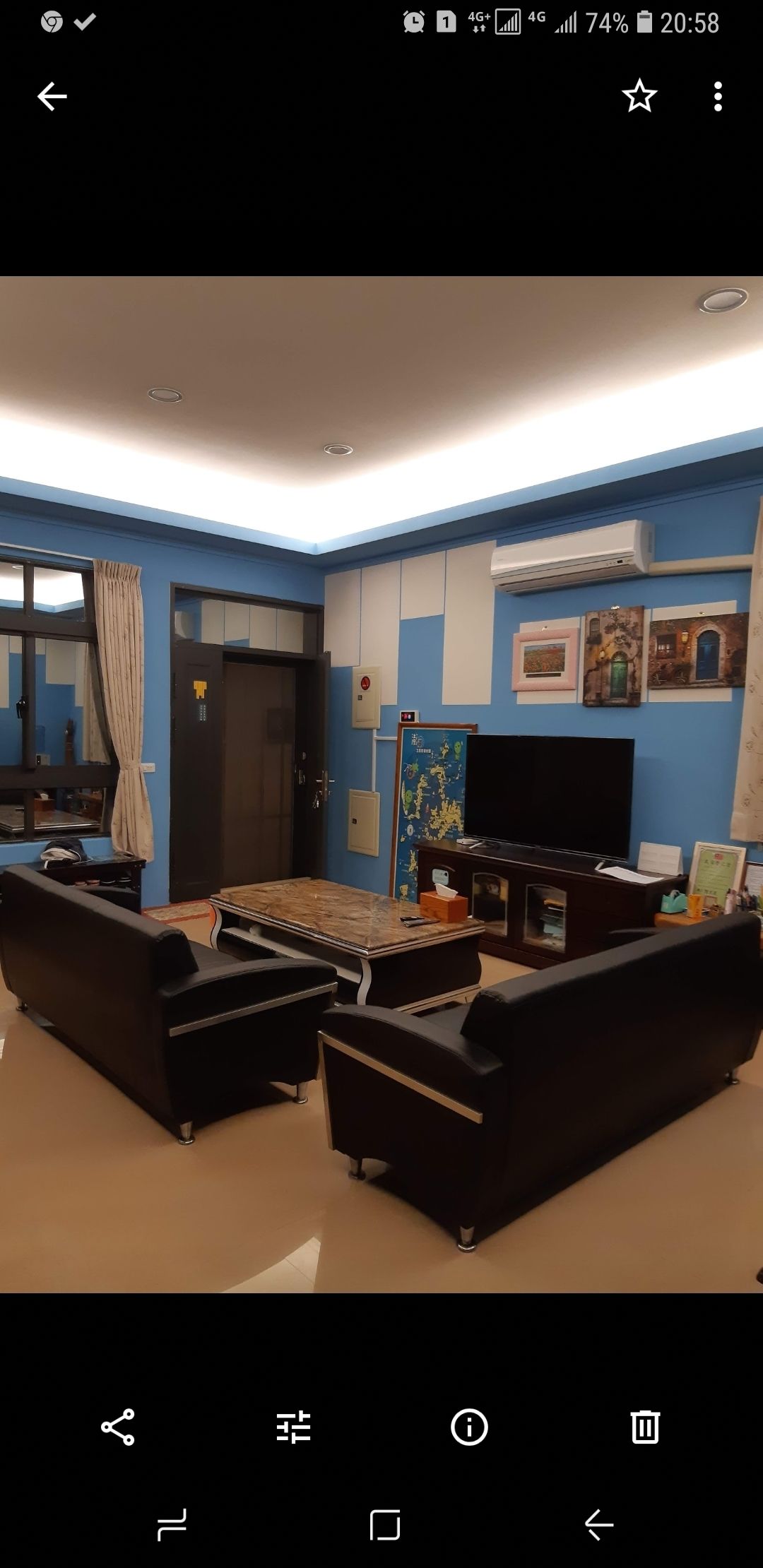 Uma sala de estar moderna com televisão de tela plana, sofás pretos, uma mesinha de centro e um mapa na parede.