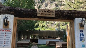 Entrada do Motel Kidrak, com uma placa, um caminho que leva ao edifício e montanhas ao fundo.